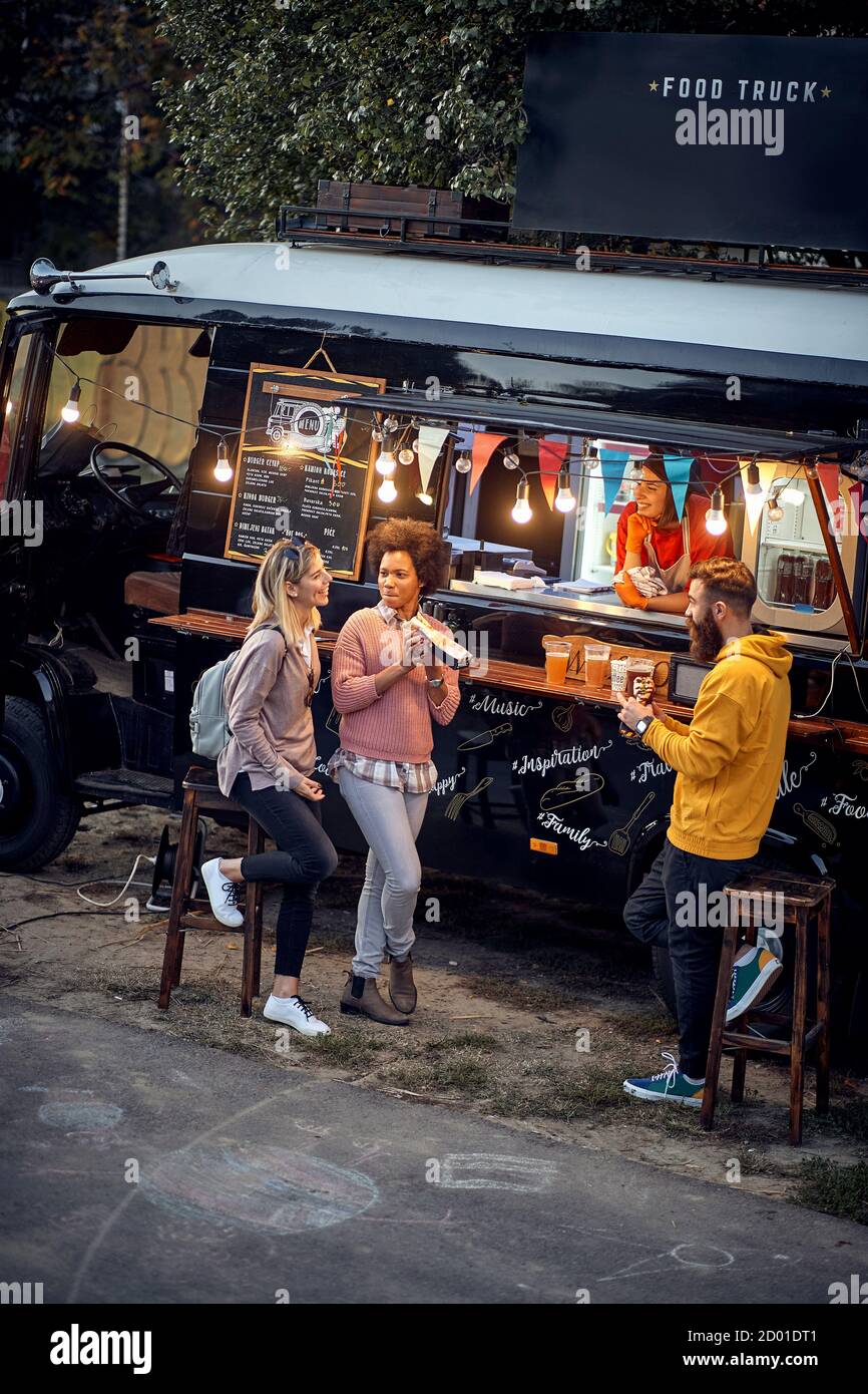 Group of friends having a meal together in front of food truck; Urban ...
