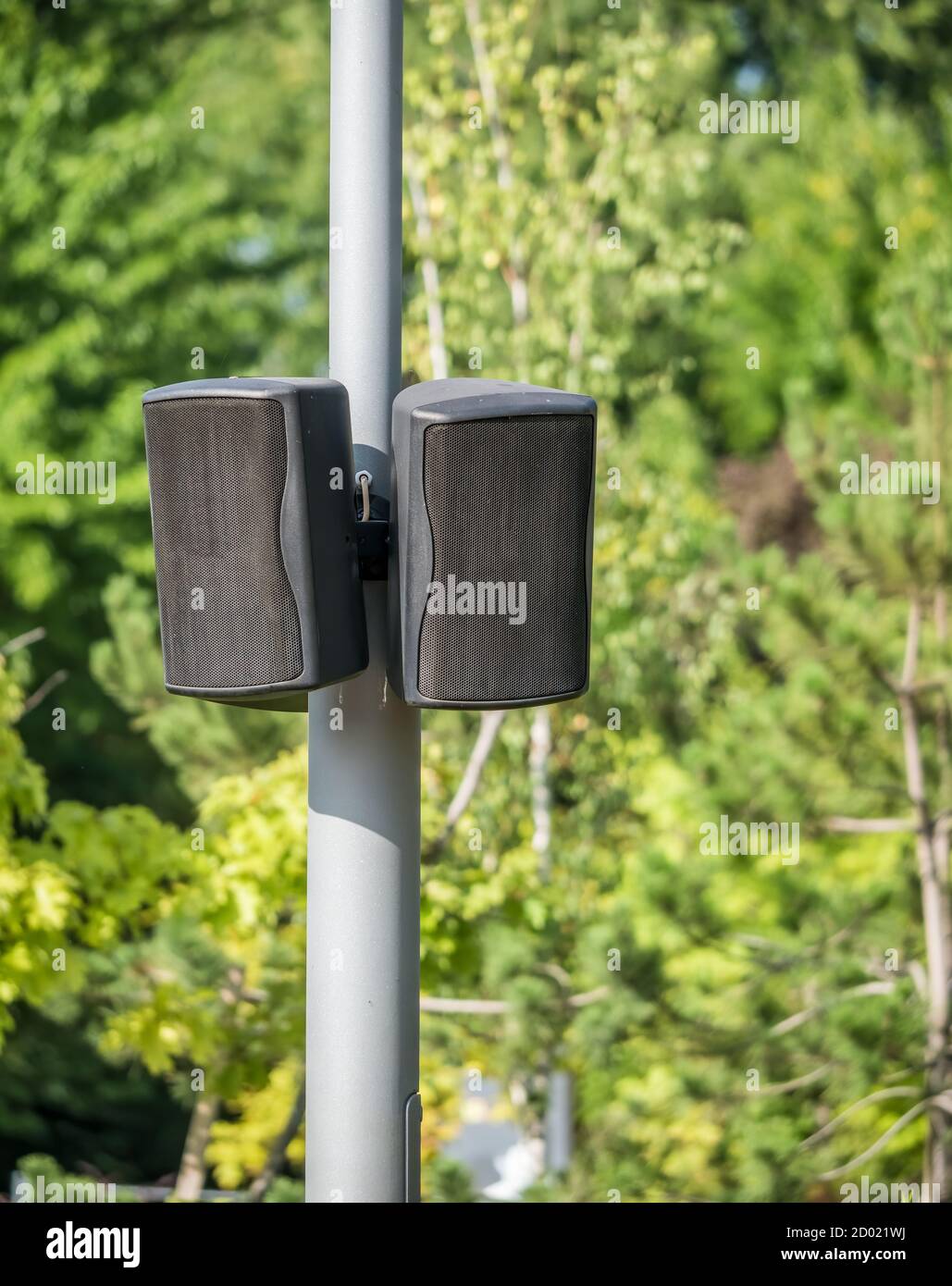 Black speakers suspended from a metal pole with blue sky as a background. Outdoor speakers for ...