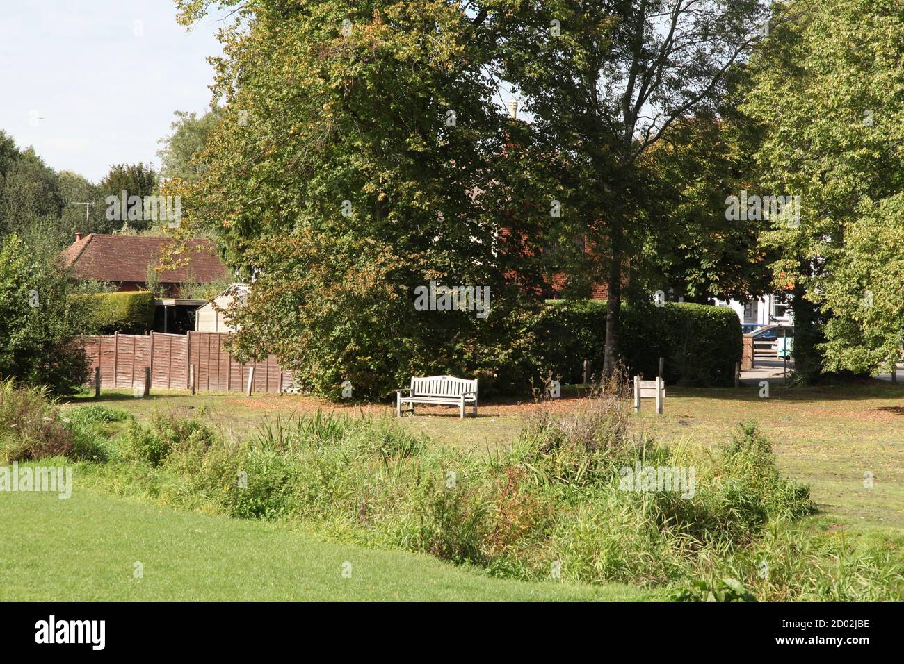 A single empty bench on the village green riverbank of Tillingbourne ...