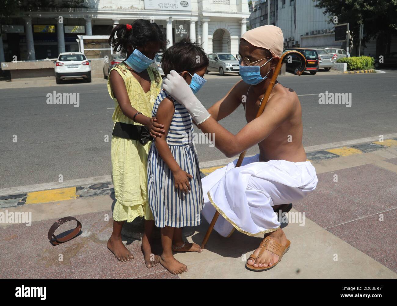 A volunteer dressed up as Mahatma Gandhi helps a child to wear a face ...