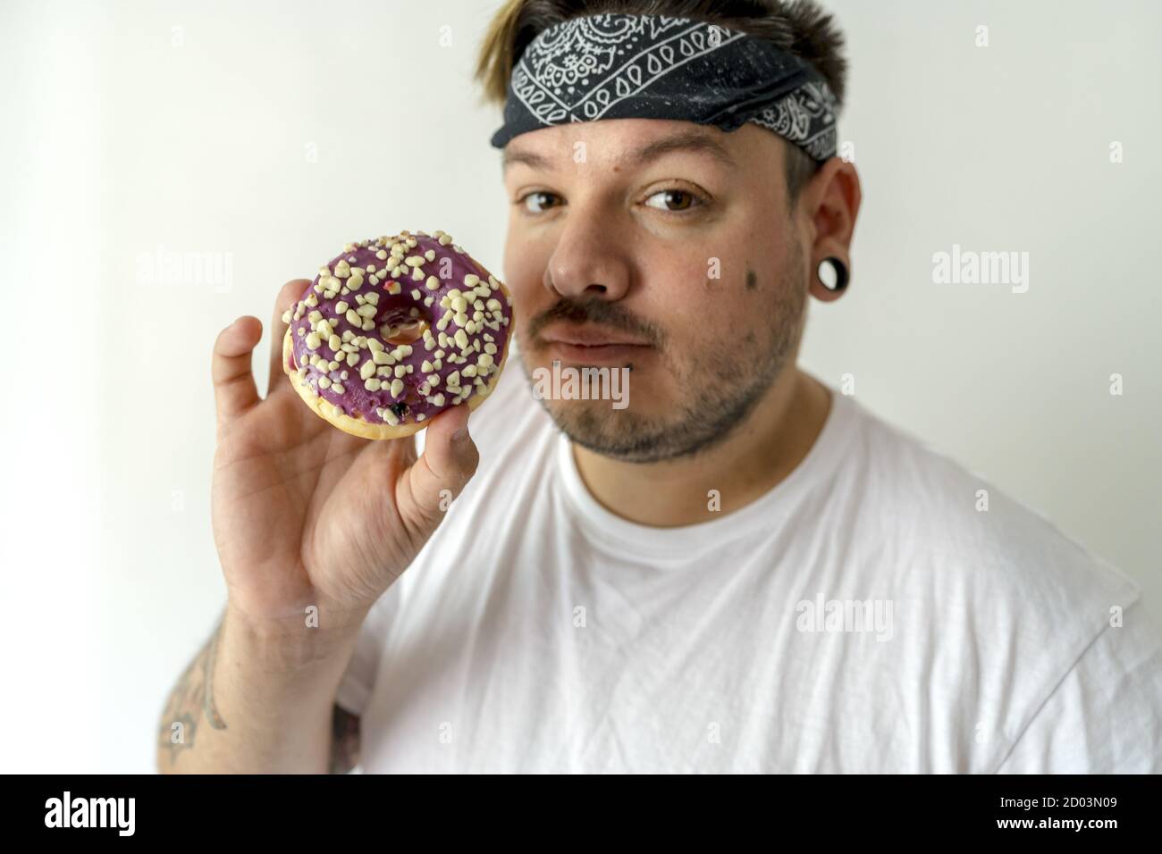 Young Caucasian male holding a delicious donut standing against a white ...