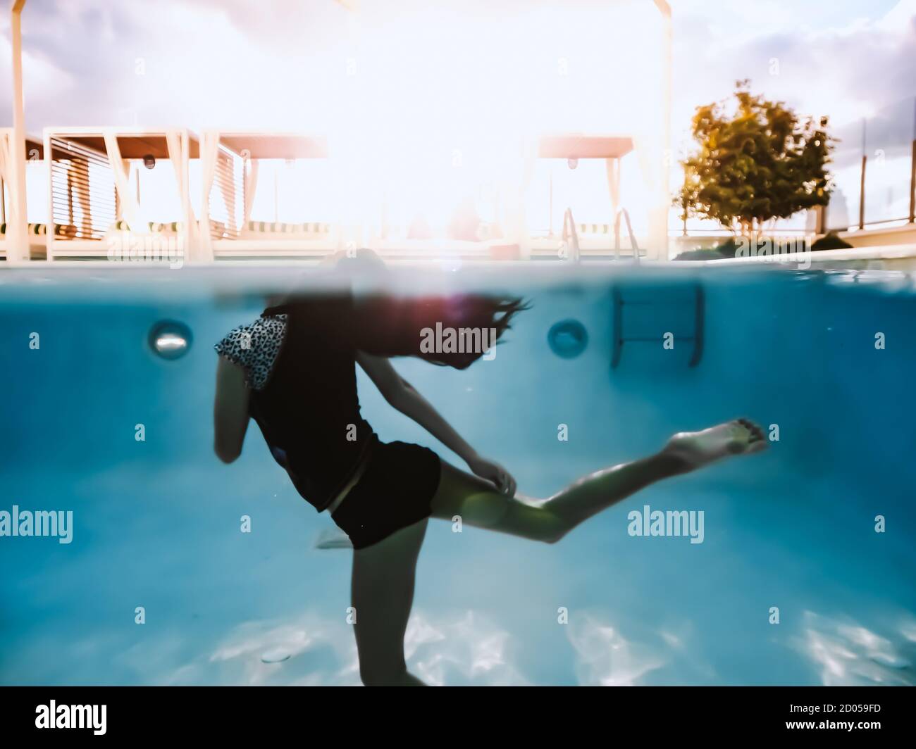 Split Shot Of Girl Leaping Underwater And The Poolside Cabanas Above