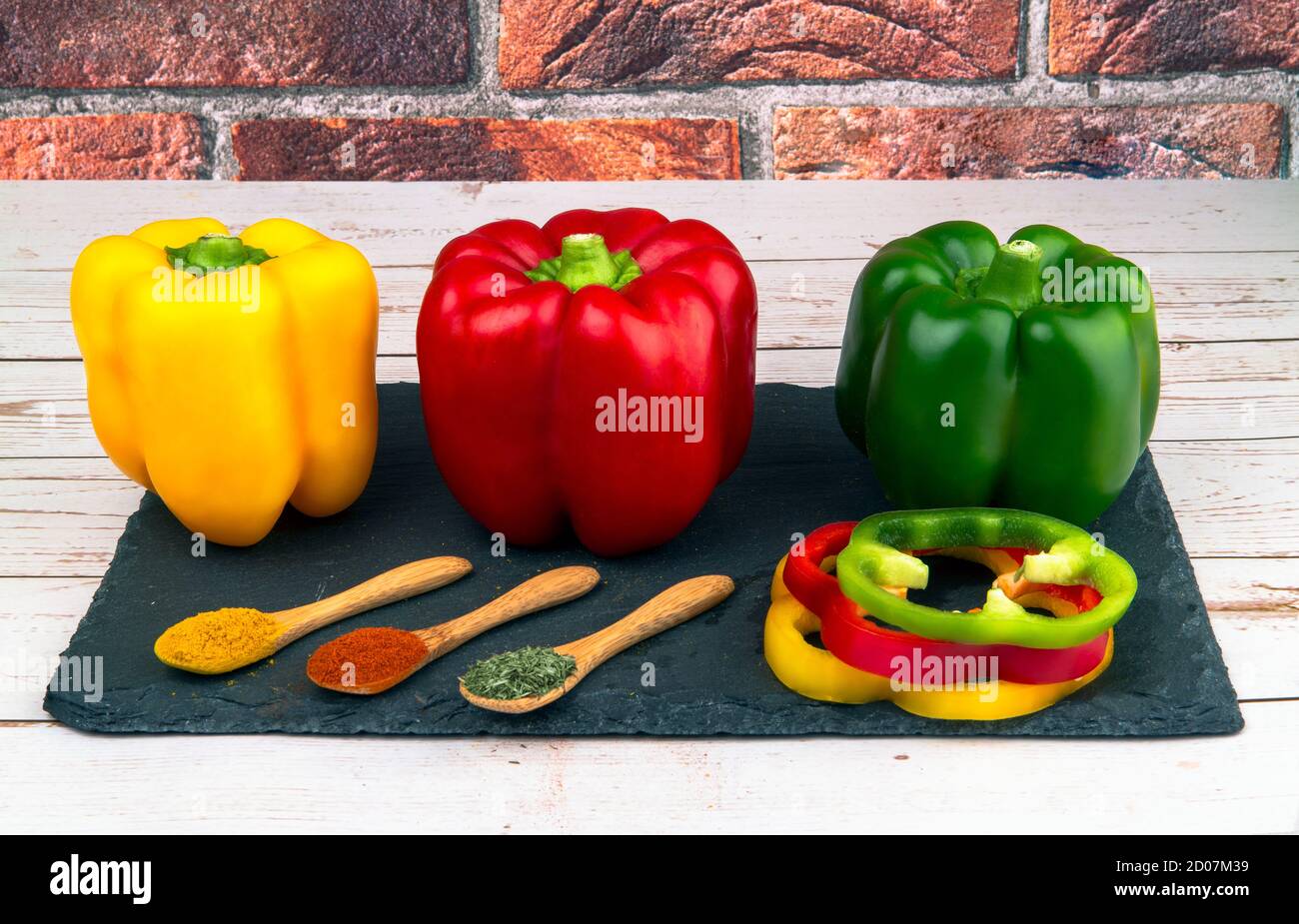 Whole and sliced red, green, yellow peppers and three wooden spoons ...