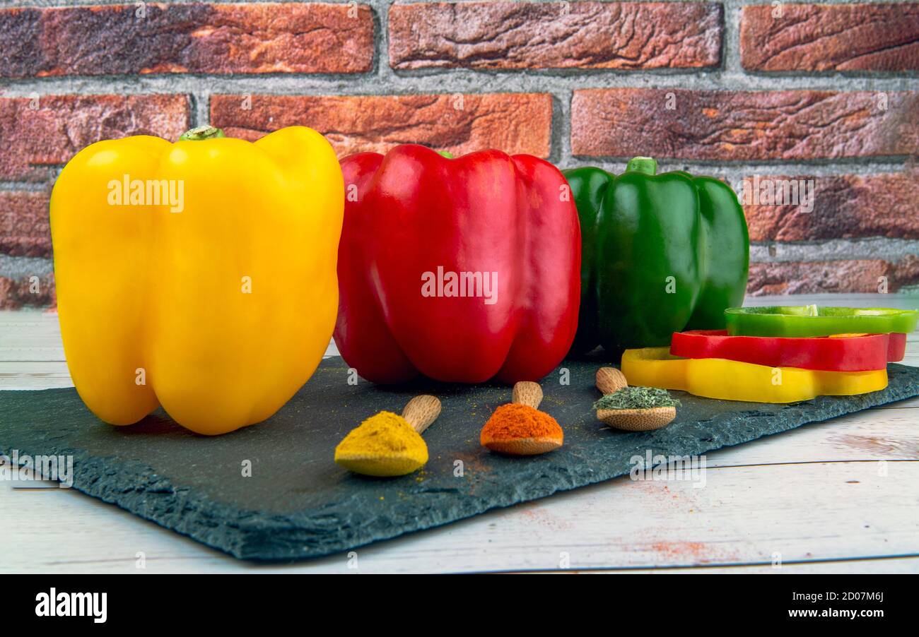 Whole and sliced red, green, yellow peppers and three wooden spoons ...