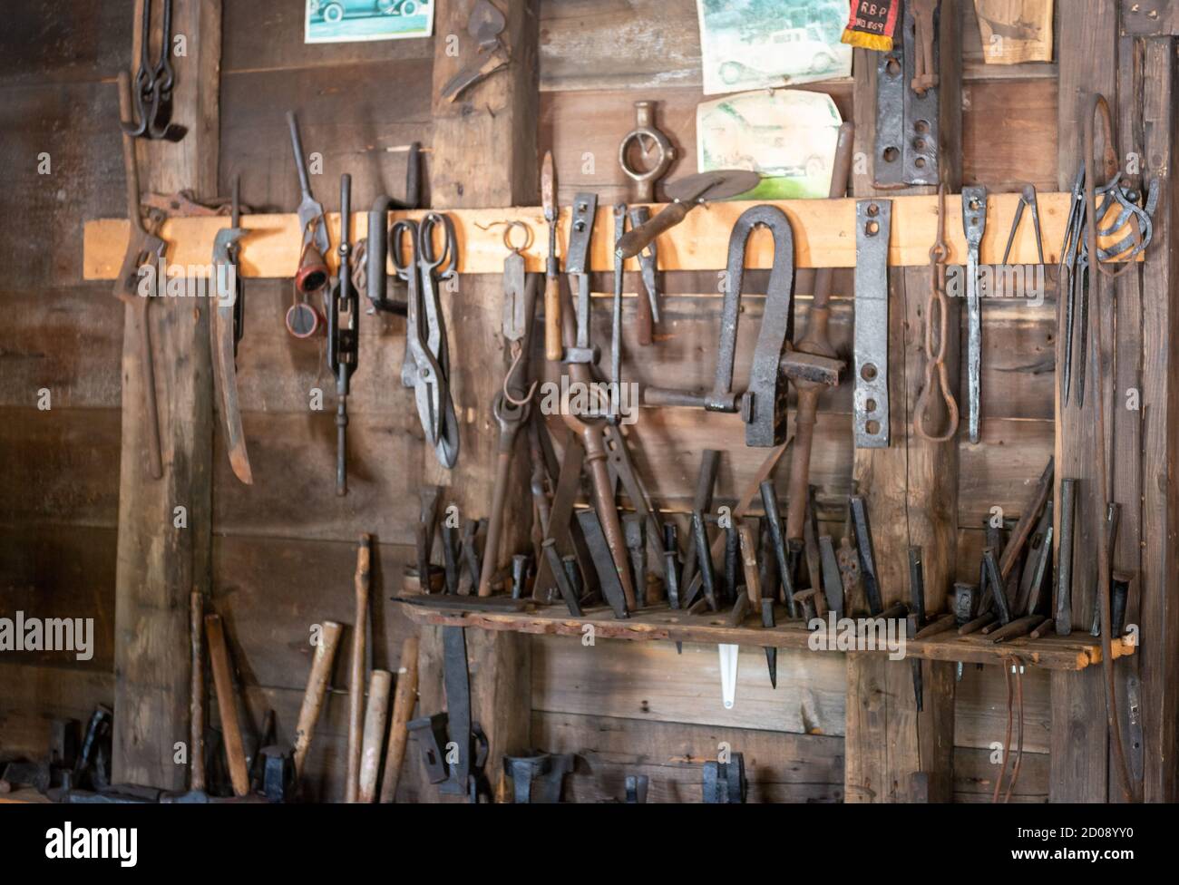 A collection of vintage blacksmith tools hung on racks on a wooden wall ...
