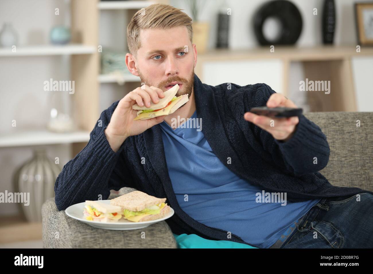 man changing tv channel with remote control while eating sandwich Stock ...