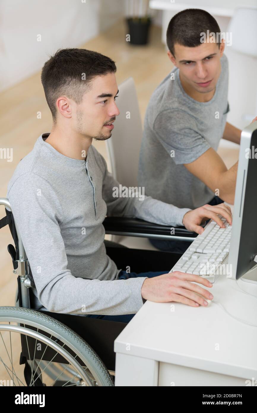 two young men using computers one in wheelchair Stock Photo - Alamy