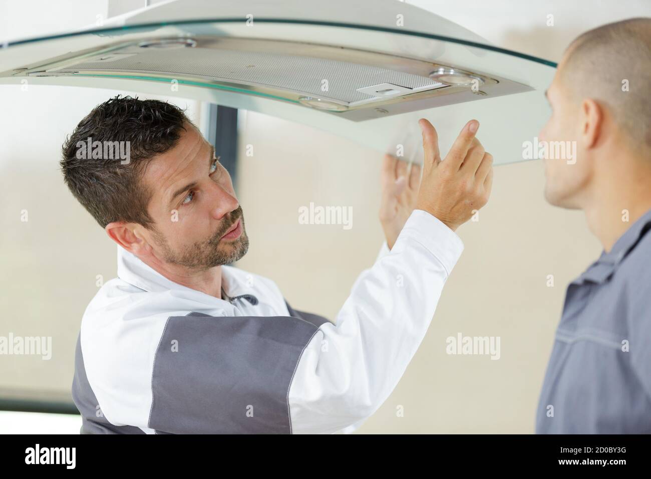 two workmen installing domed glass extractor hood Stock Photo - Alamy
