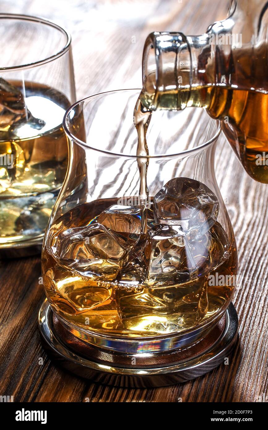 Pouring whisky from a bottle into a glass with ice cubes Stock Photo ...