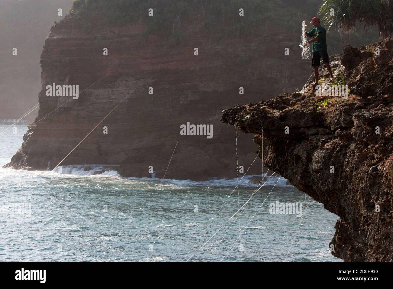 A fisherman fixes nets on rocks to catch lobsters at Timang beach in ...