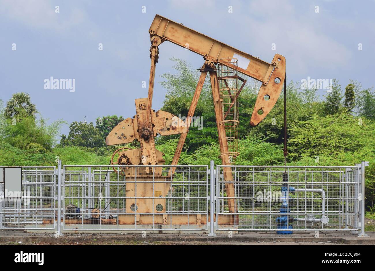 Old isolated rusty oil pump jack extracting crude oil and natural gas from well in green and ...