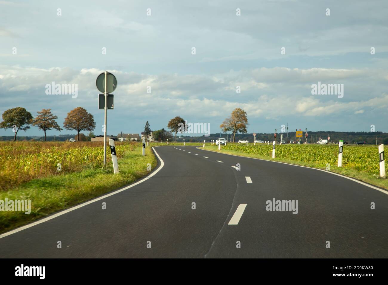 curvy country roud with cars in the distance, between fields, asphalt ...