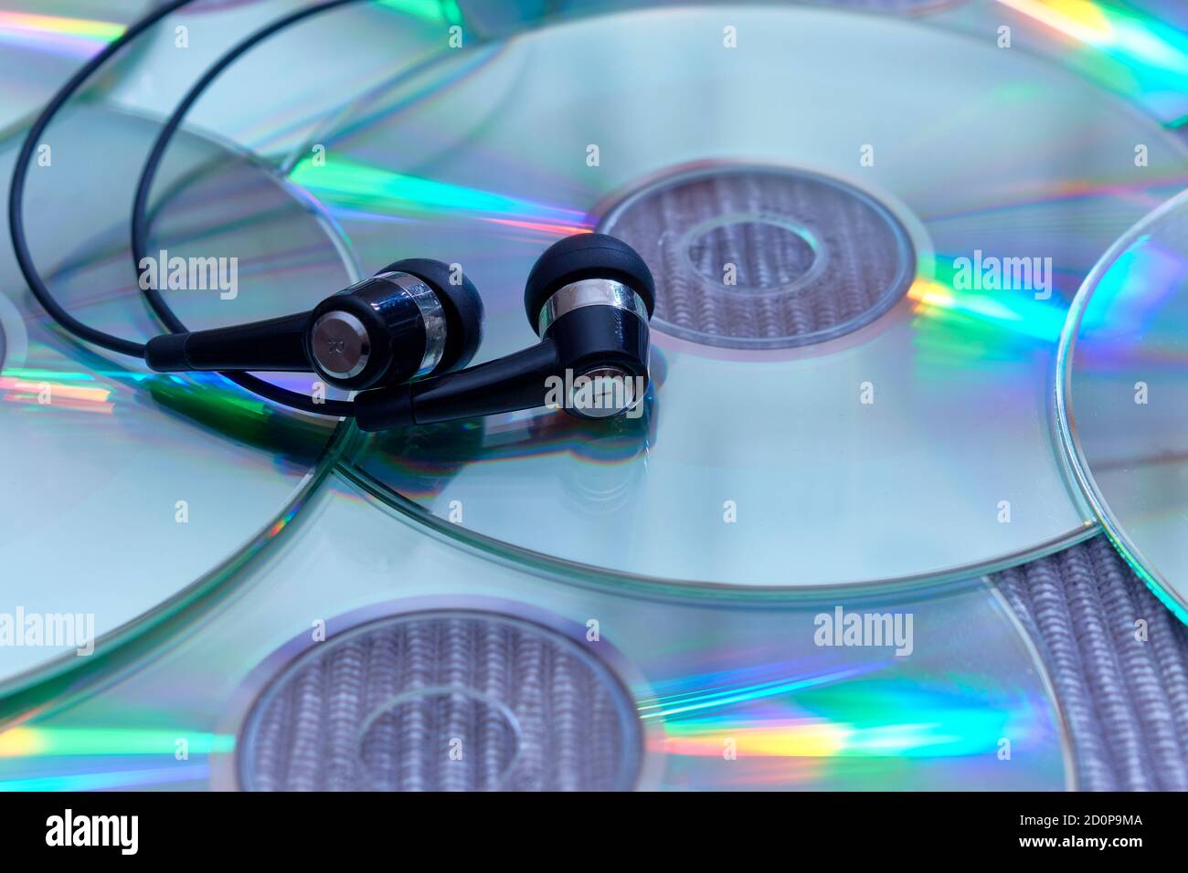 Black audio headphones on a pile of glossy compact discs with colored ...