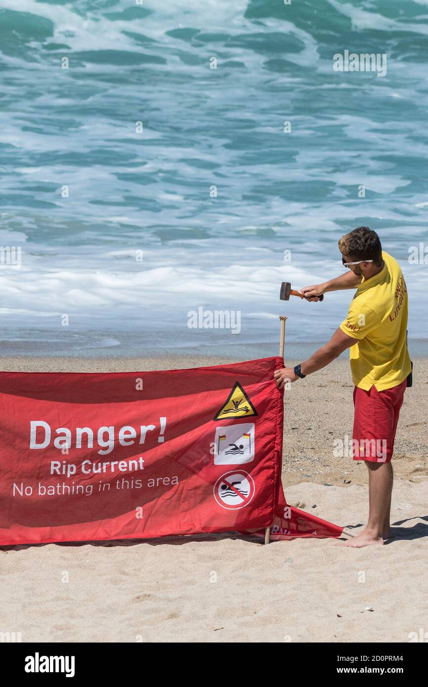 An RNLI Lifeguard putting up a warning sign on Fistral Beach in Newquay ...