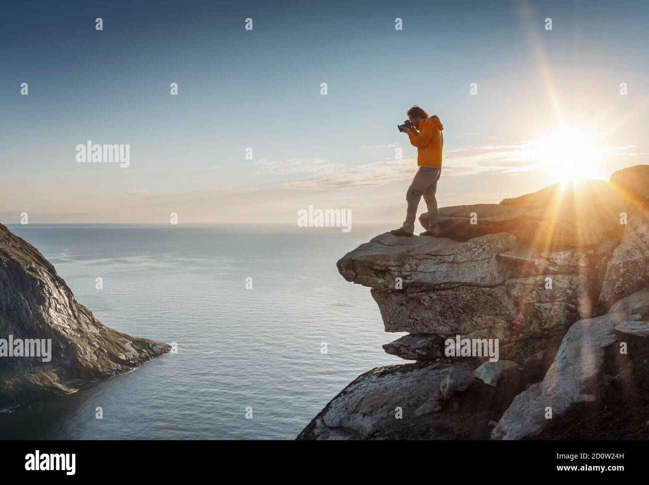 Photographer in front of sun on rocky outcrop, behind ocean, Ryten ...
