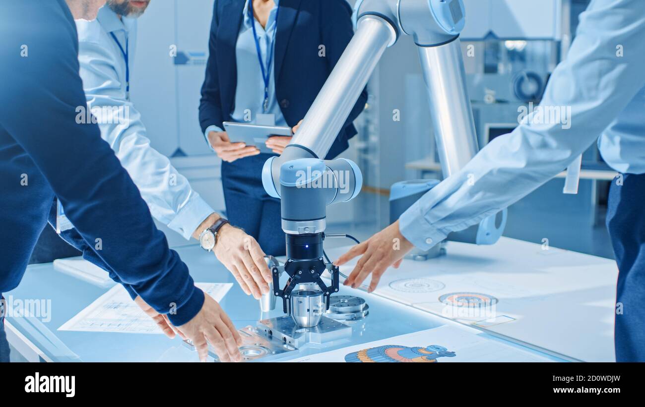 Team of Industrial Robotics Engineers Gathered Around Table With Robot ...