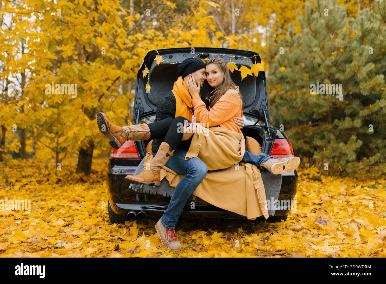A cute young couple in love is sitting in a car with the trunk open ...