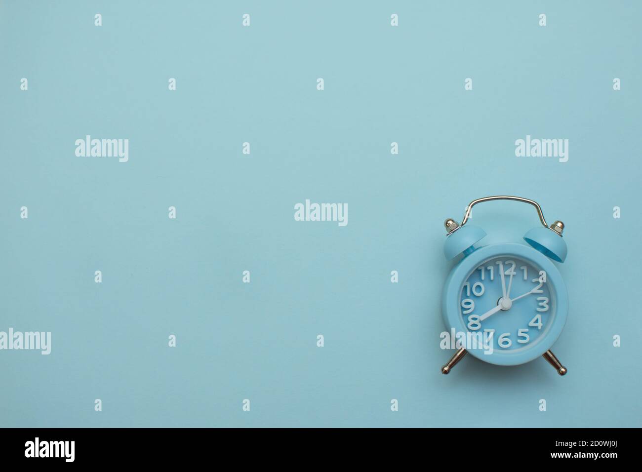 blue clock alarm clock on a light blue background, place for an ...