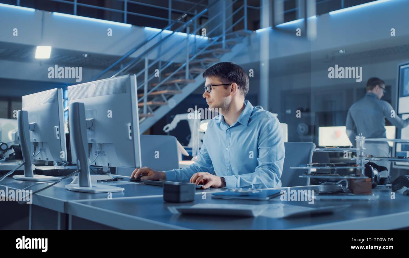 Electronics Development Engineer Sitting at His Desk Uses personal ...