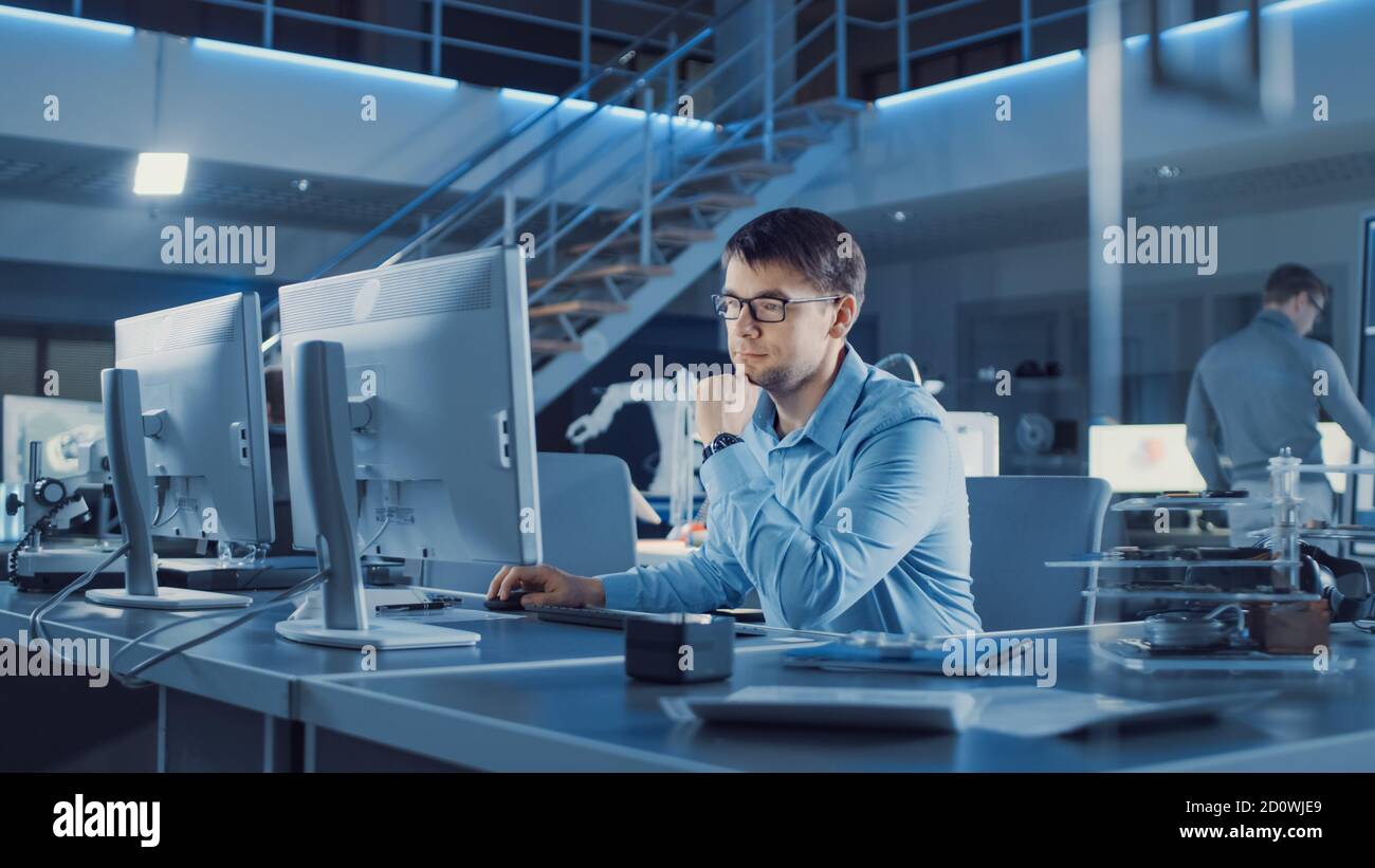 Electronics Development Engineer Sitting at His Desk Uses personal ...