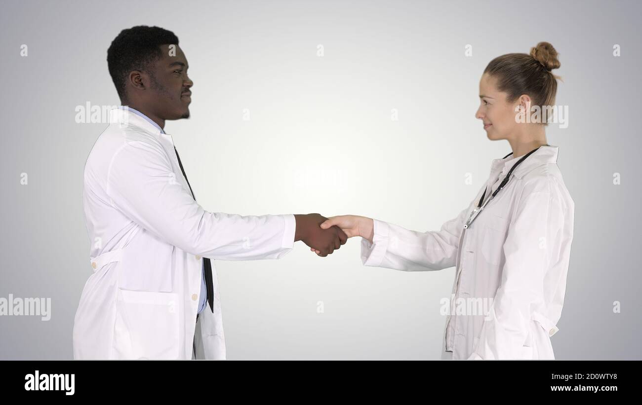Two young doctor shaking hands on gradient background Stock Photo - Alamy