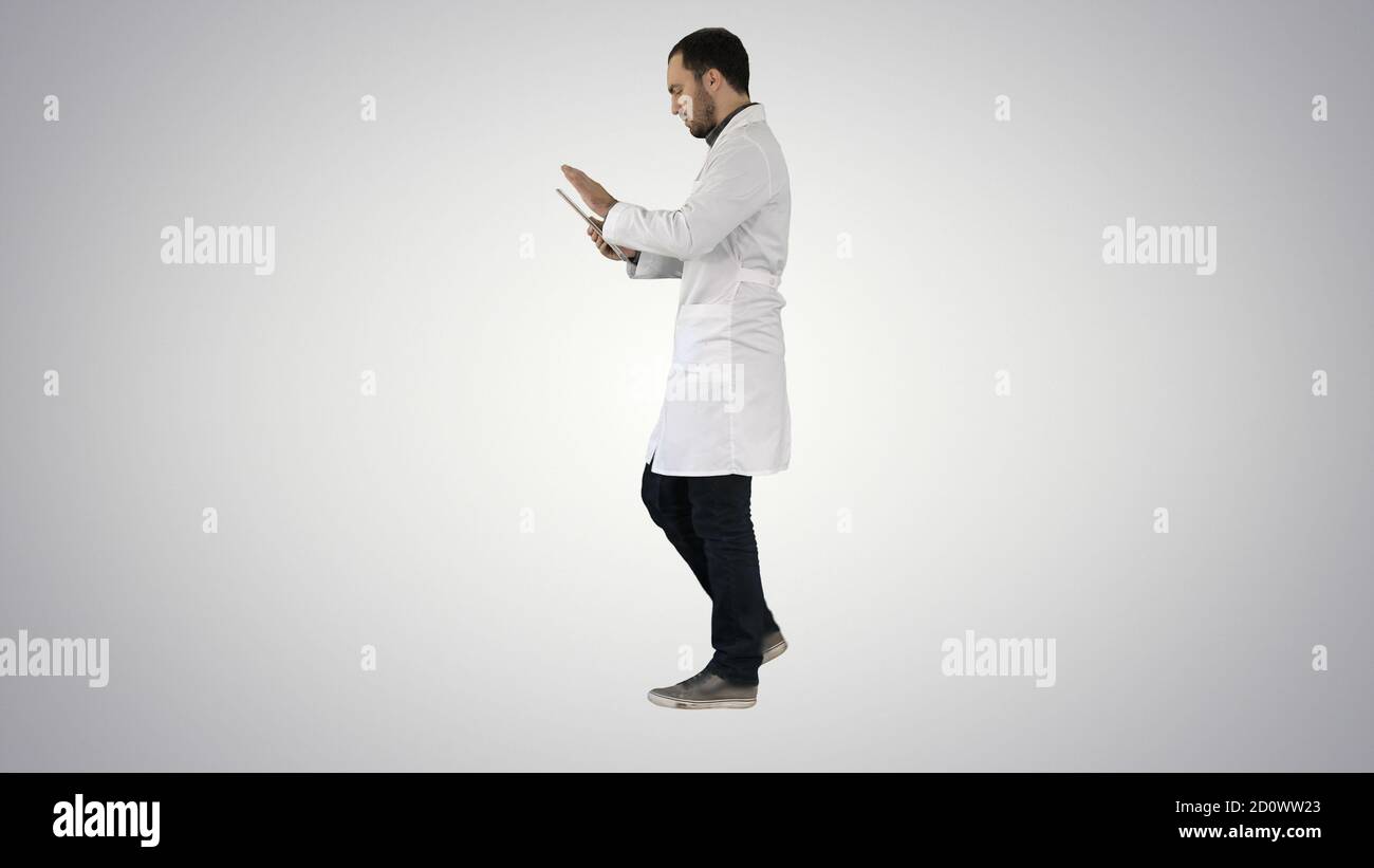 Doctor using tab while walking on gradient background Stock Photo - Alamy