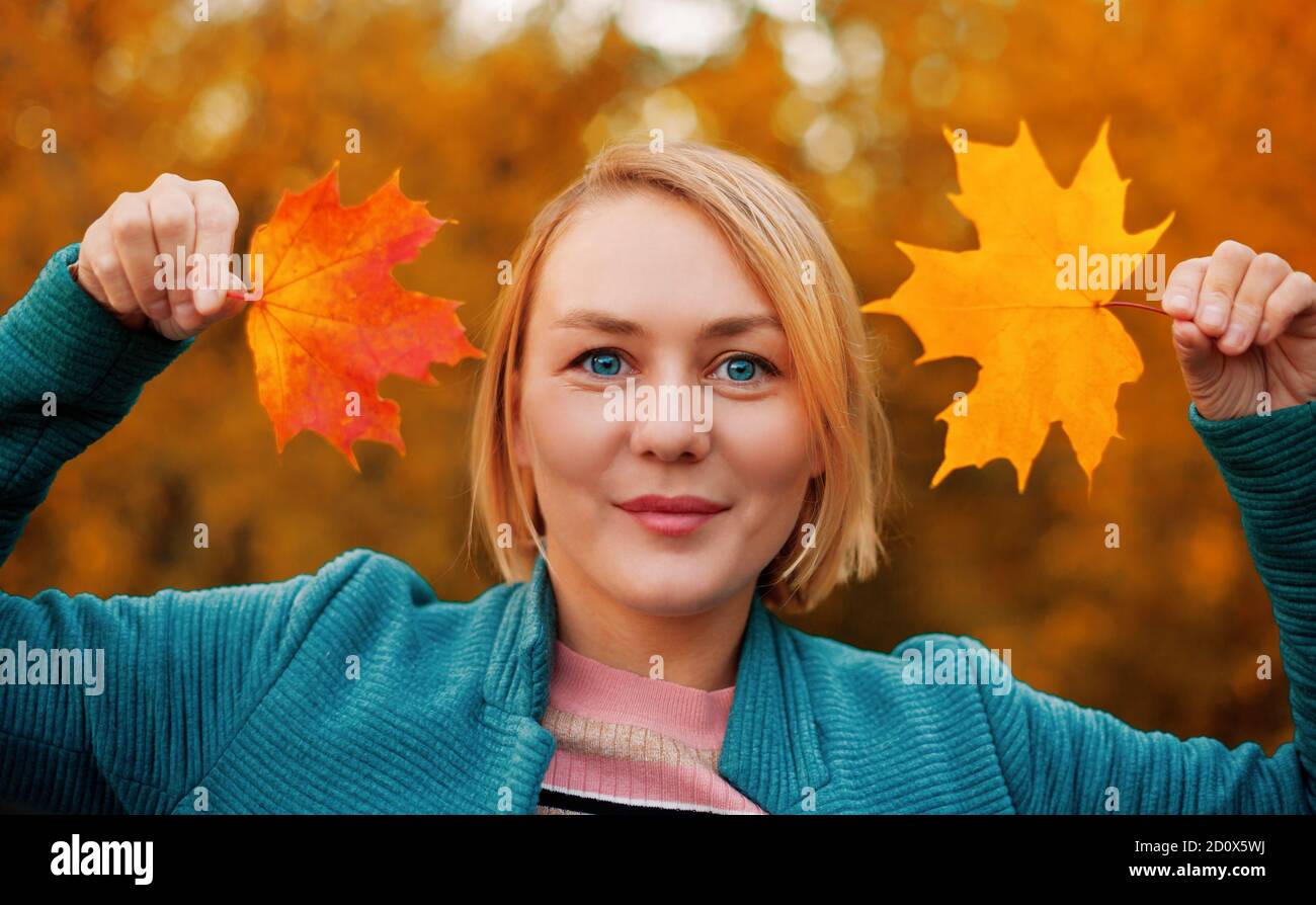 Smiling playful woman holding maple leaves in her hands from both sides ...