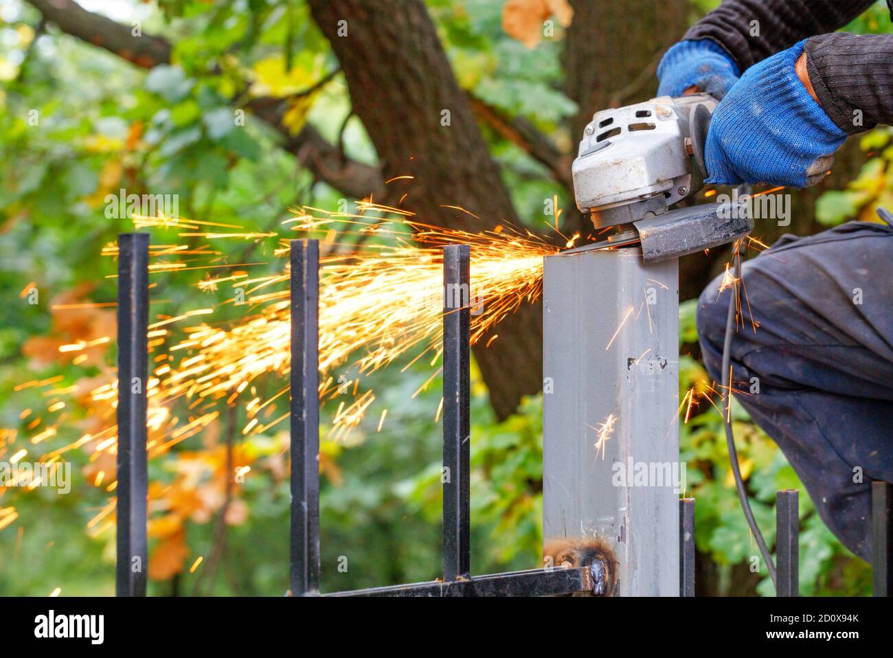 An industrial worker cuts a metal post with a disc angle grinder ...