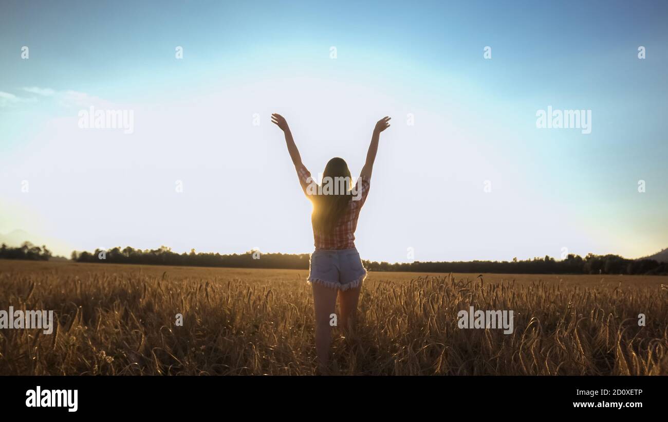 Happy woman walking on a wheat field with open arms at the bright sun ...