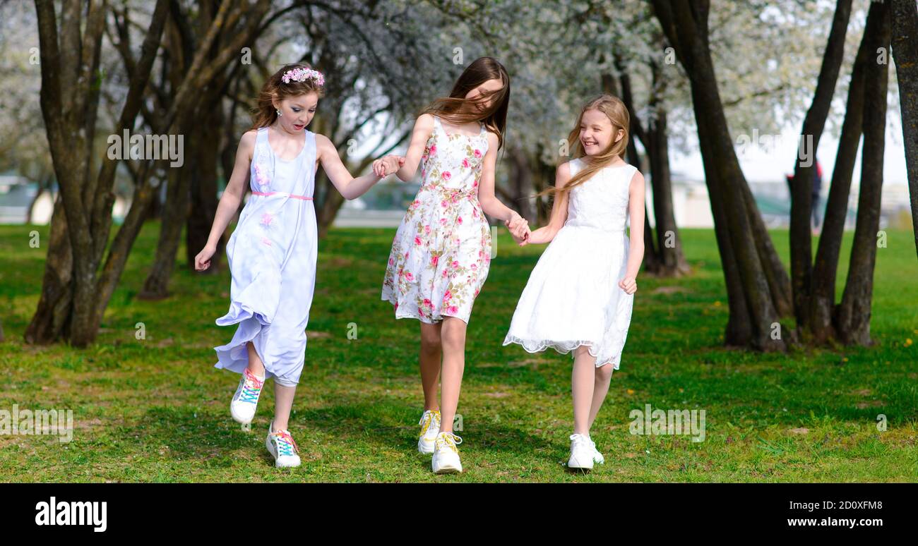 Three beautiful girls in retro dresses for a walk in a flowered garden ...