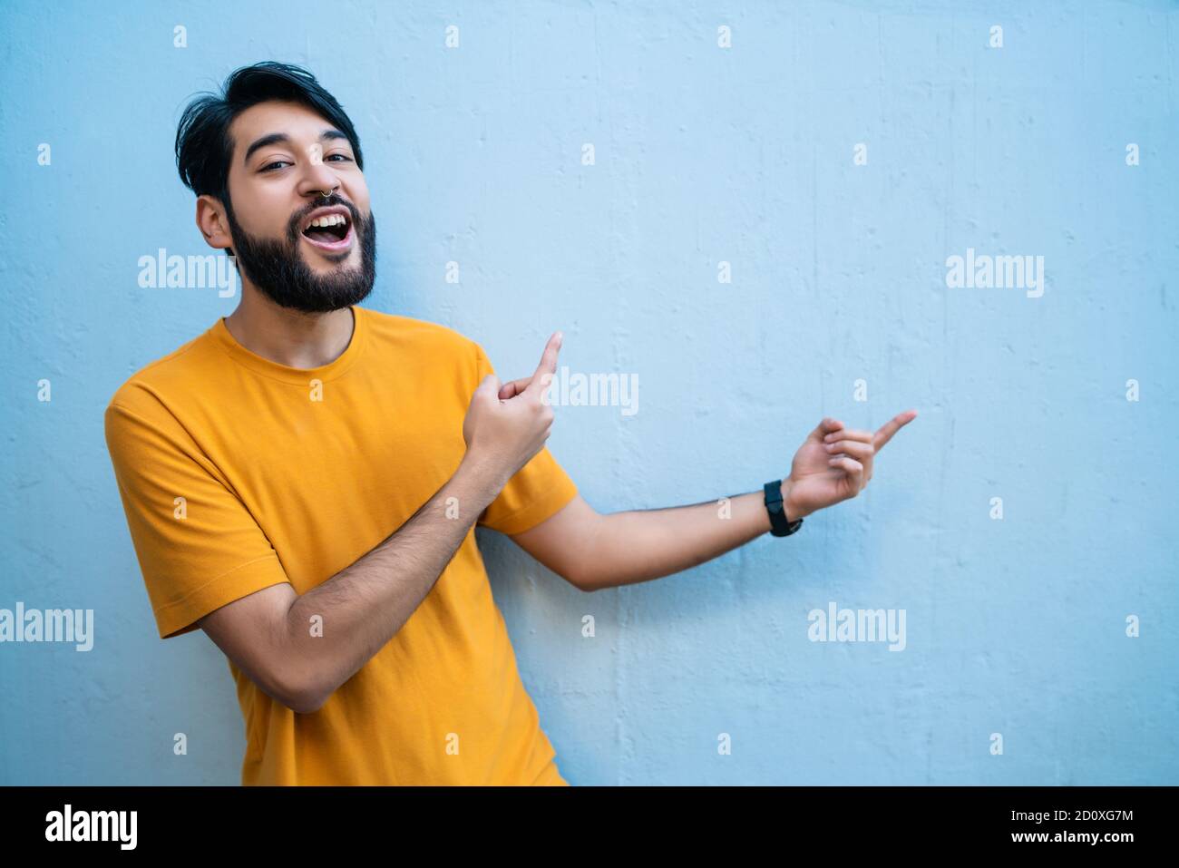 Portrait of young latin man pointing and showing something against blue ...