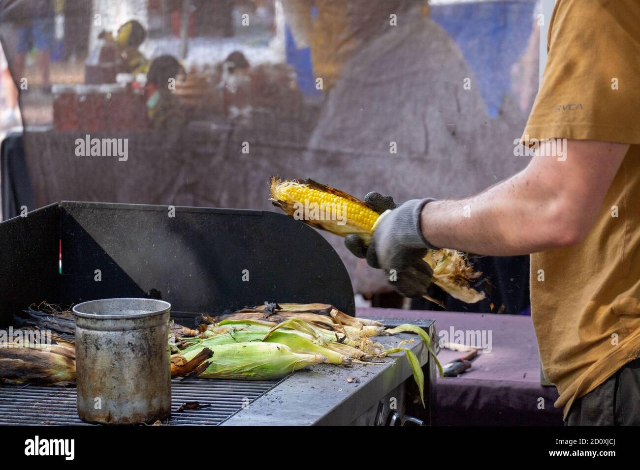 A street vendor prepares corn on the cob by basting it with melted ...