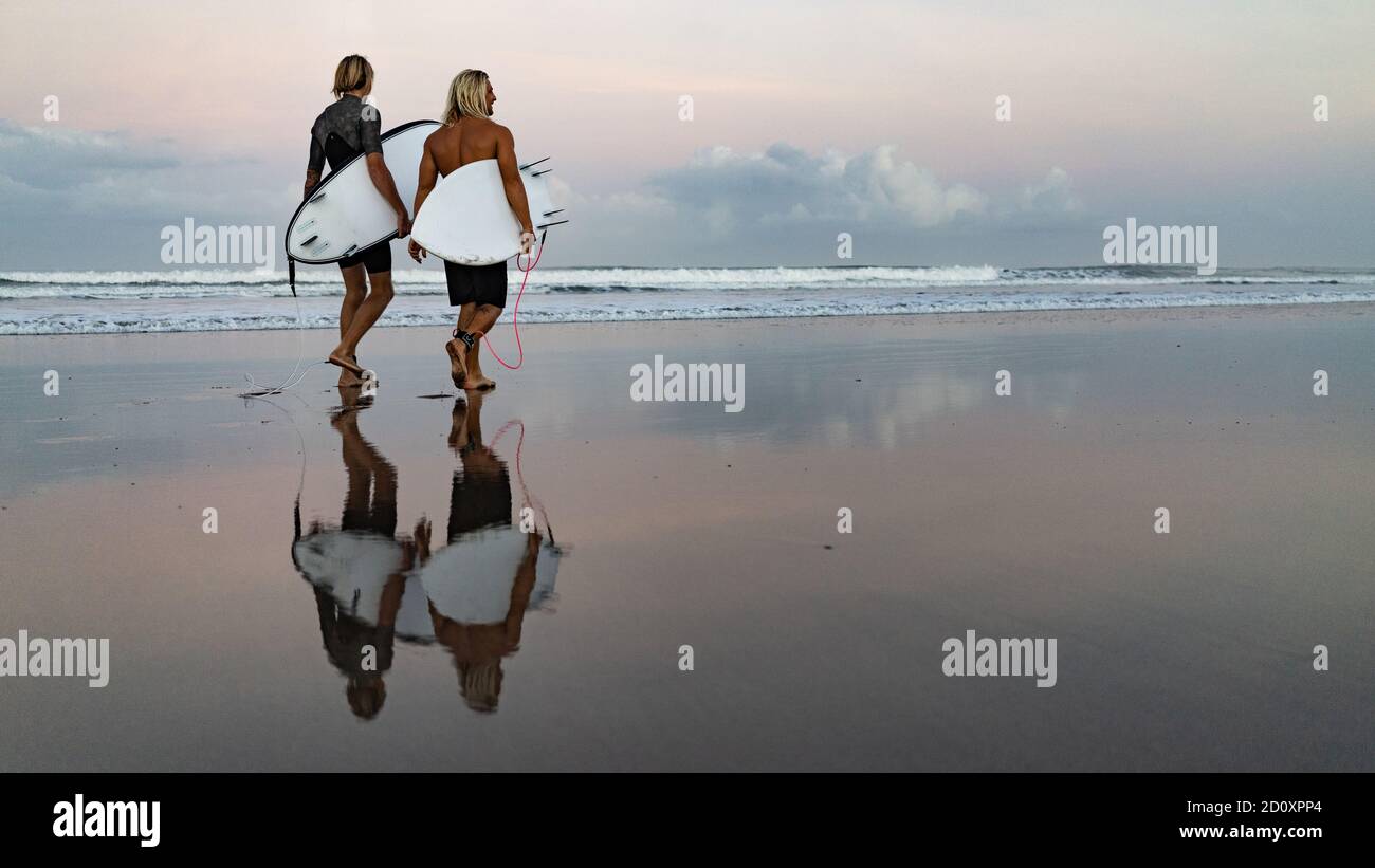 Two handsome male surfers walking on the beach with surfboards ...