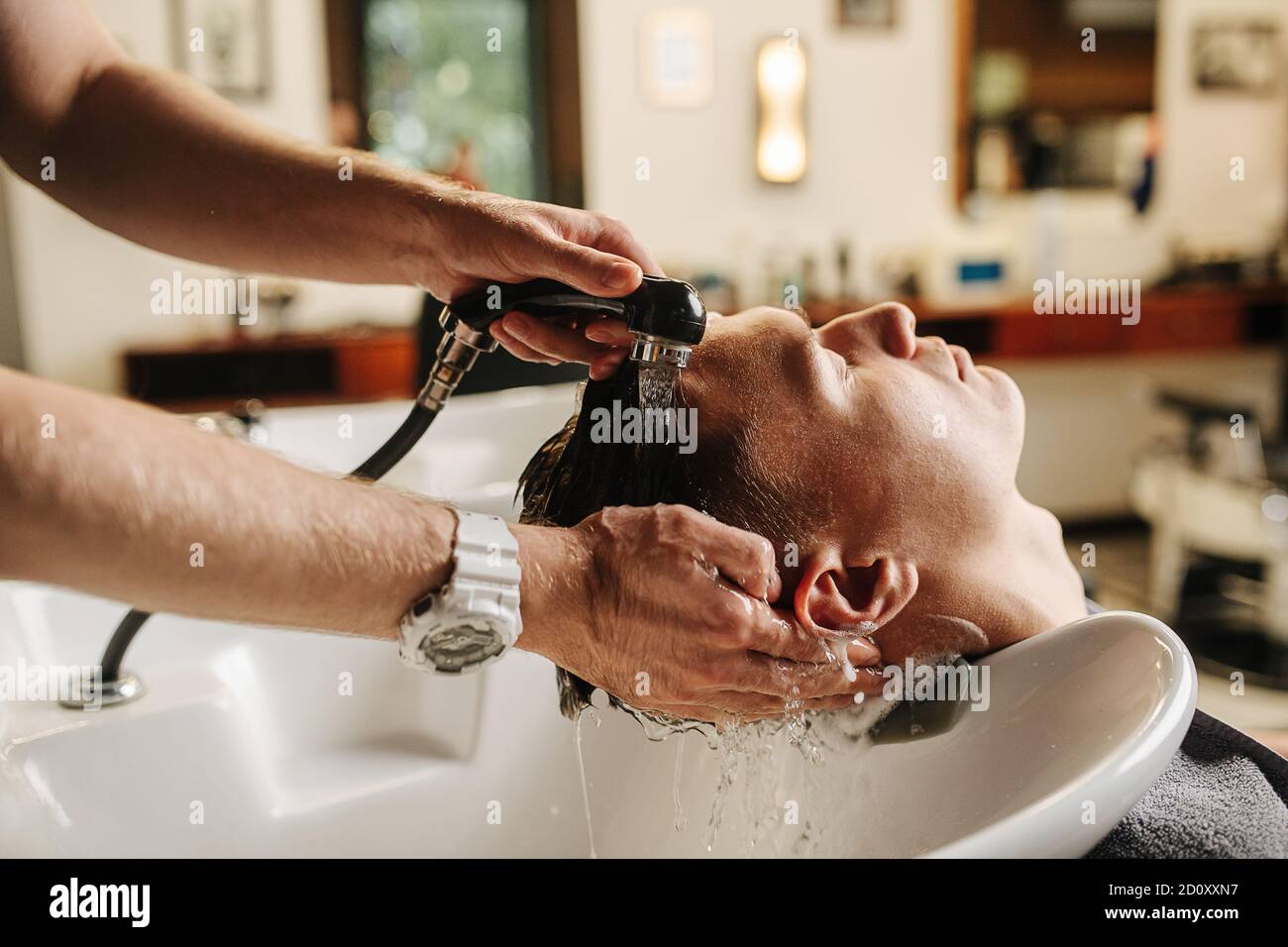 Hands washing client's head in a specialised sink in a barber shop ...