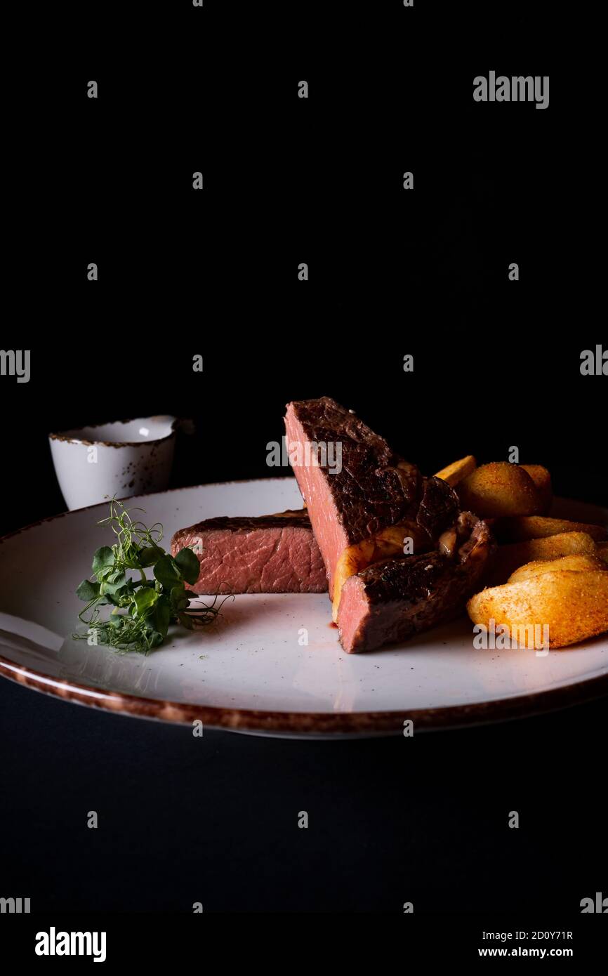 Vertical shot of beef steak with potatoes and sauce isolated on black ...