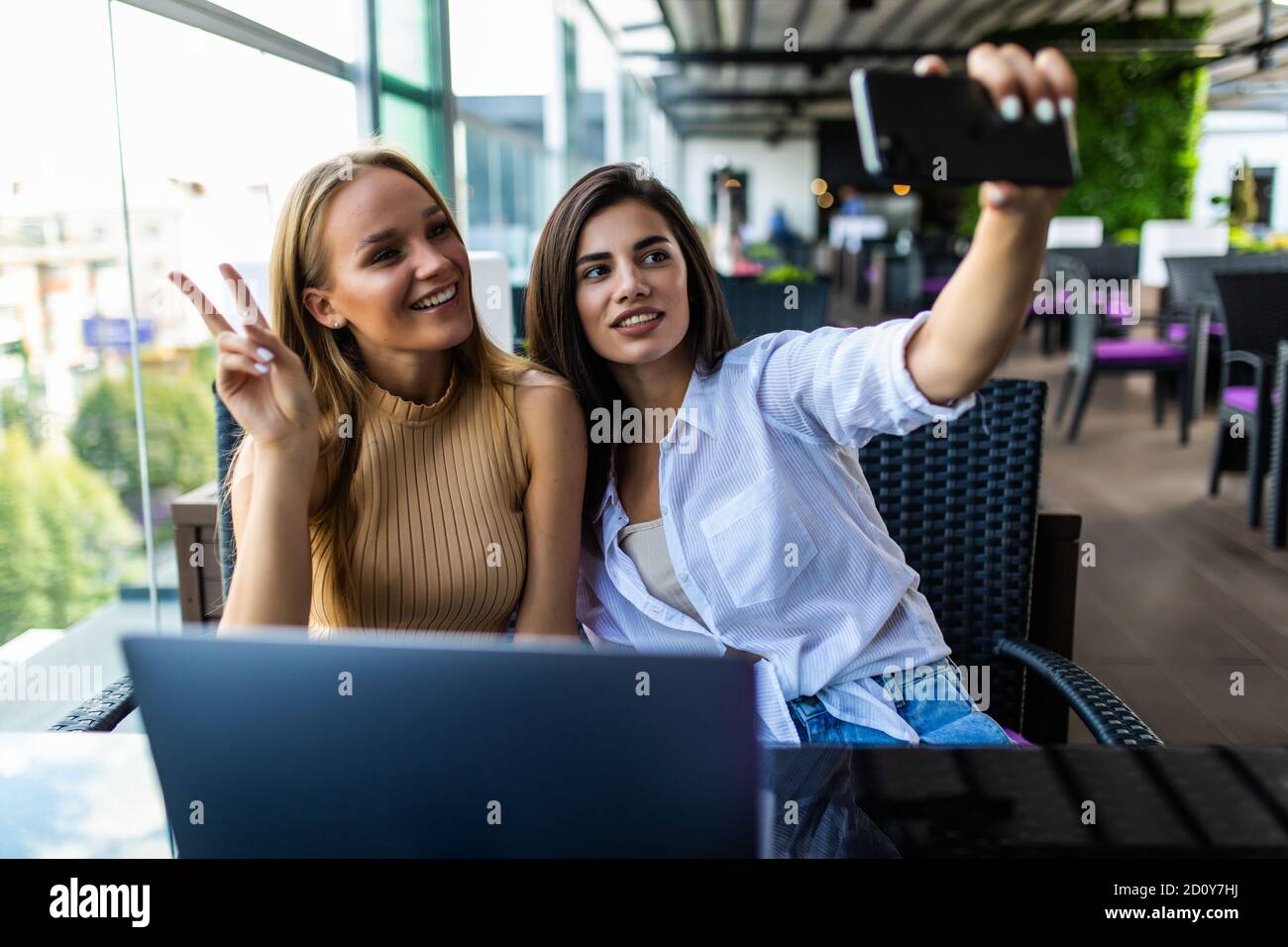 Two young attractive women making selfie photos on telephone sitting in ...