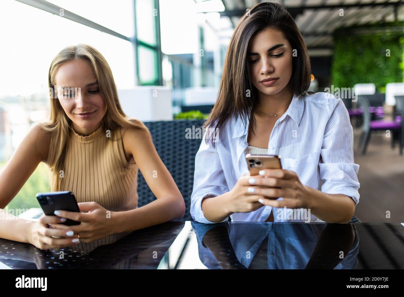 Two friends enjoying coffee together in a coffee shop and using phone ...