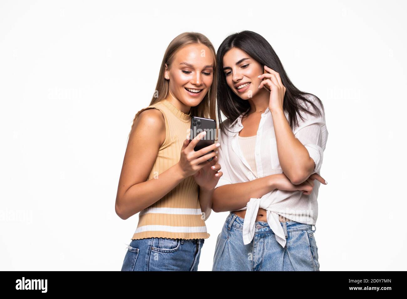 Two surprised cute young women using mobile phone together over white ...