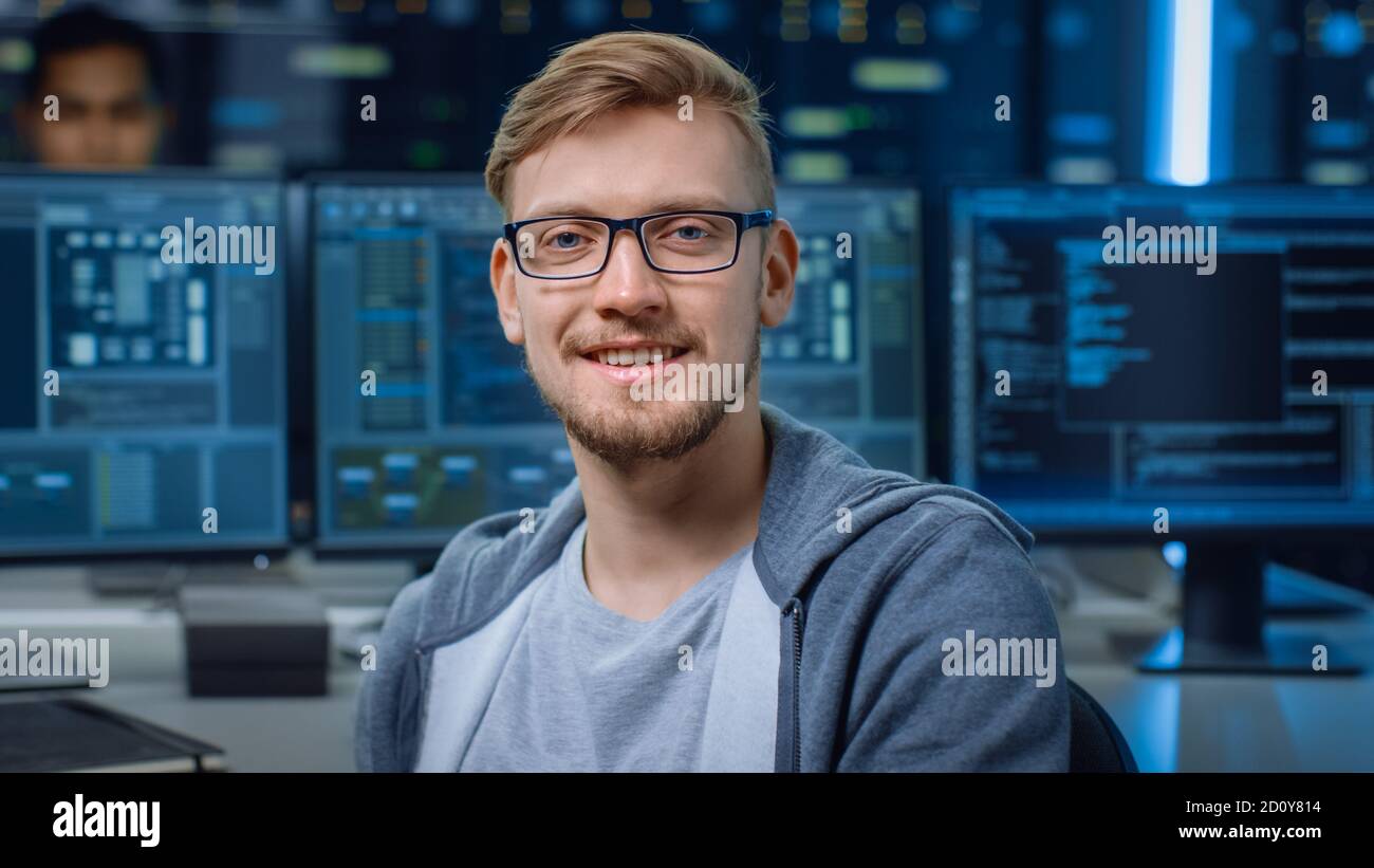 Portrait of a Smart and Handsome IT Specialist Wearing Glasses Smiles, Behind Him Personal ...