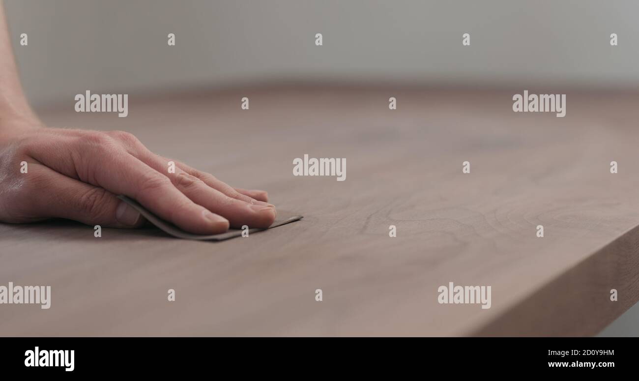 man hand sanding toned walnut table surface before applying finish ...