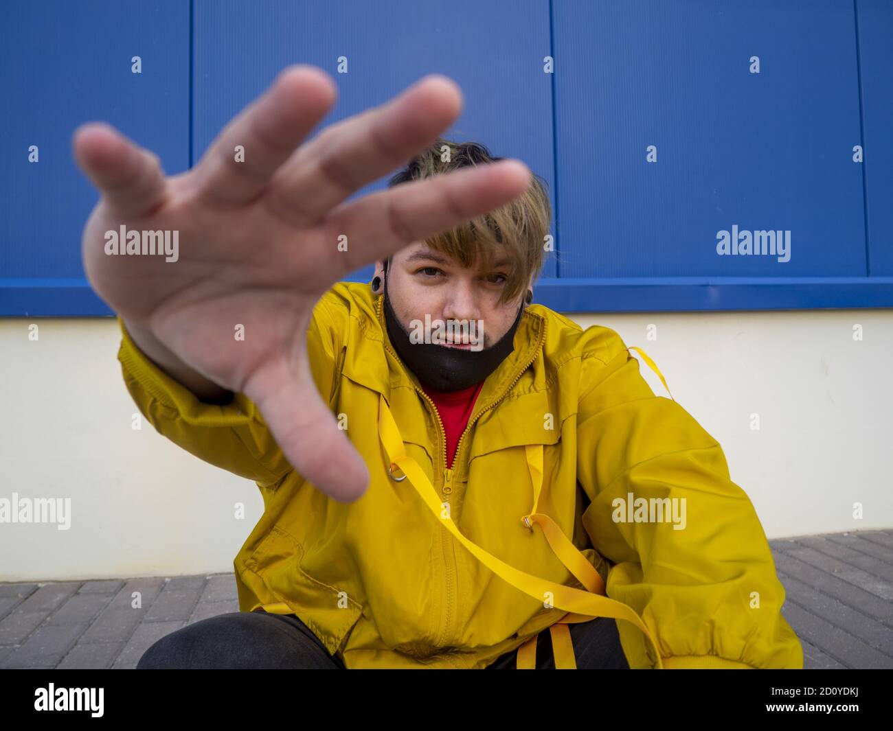Male wearing a yellow jacket and a mask reaching for the camera Stock ...