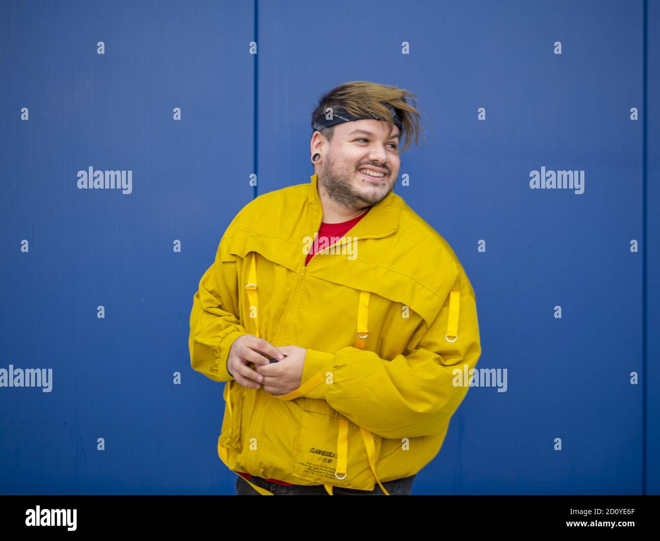 Male wearing a yellow jacket and posing by a blue wall Stock Photo - Alamy