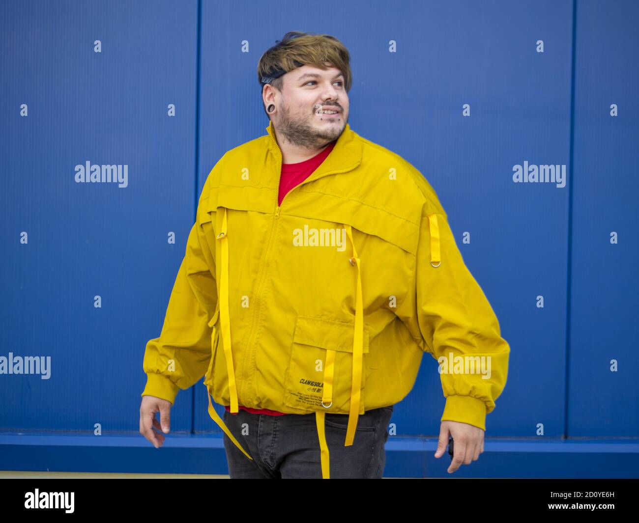 Male wearing a yellow jacket and posing by a blue wall Stock Photo - Alamy