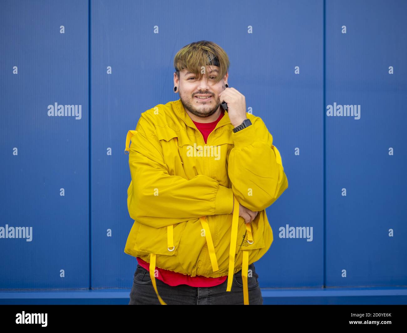 Male wearing a yellow jacket and posing by a blue wall Stock Photo - Alamy