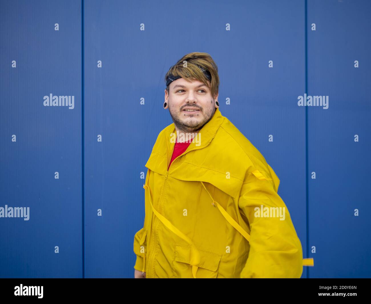 Male wearing a yellow jacket and posing by a blue wall Stock Photo - Alamy