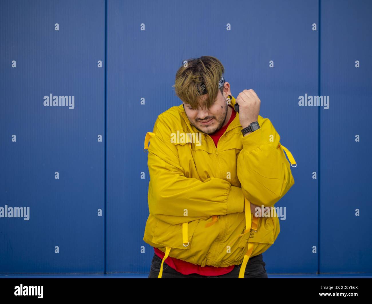 Male wearing a yellow jacket and posing by a blue wall Stock Photo - Alamy