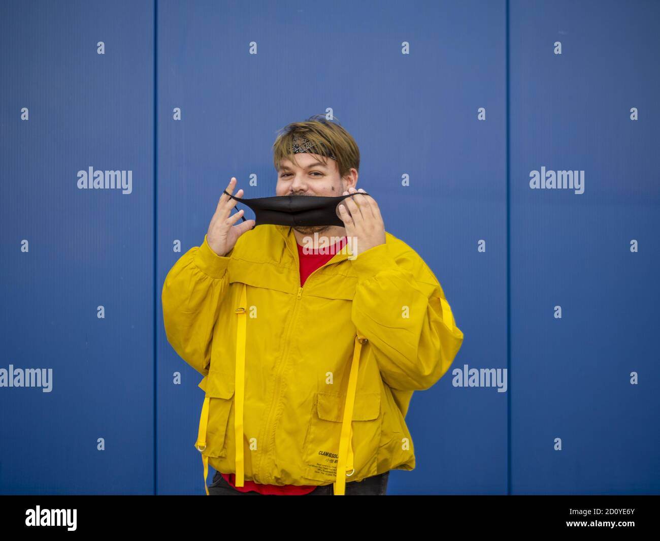 Male wearing a yellow jacket and a mask and posing by a blue wall Stock ...