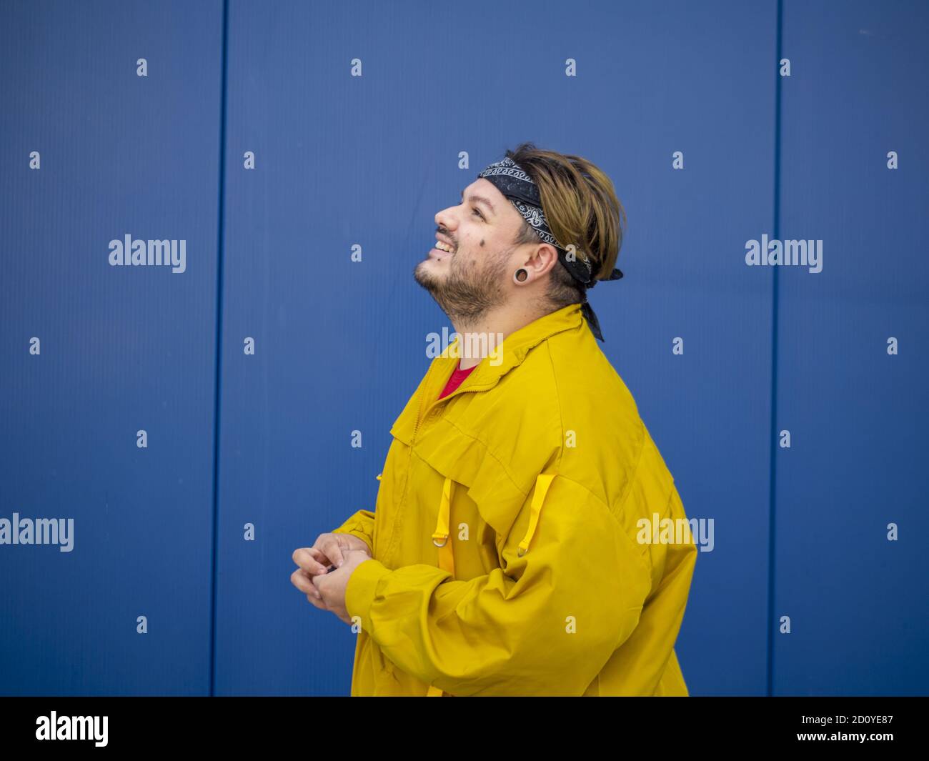 Male wearing a yellow jacket and posing by a blue wall Stock Photo - Alamy