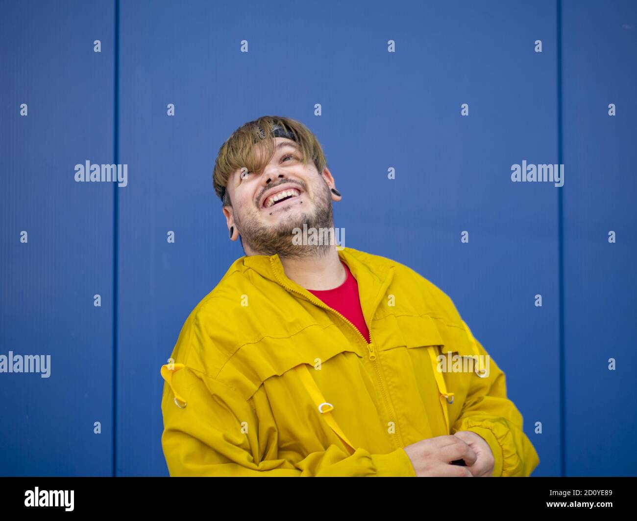Male wearing a yellow jacket and posing by a blue wall Stock Photo - Alamy
