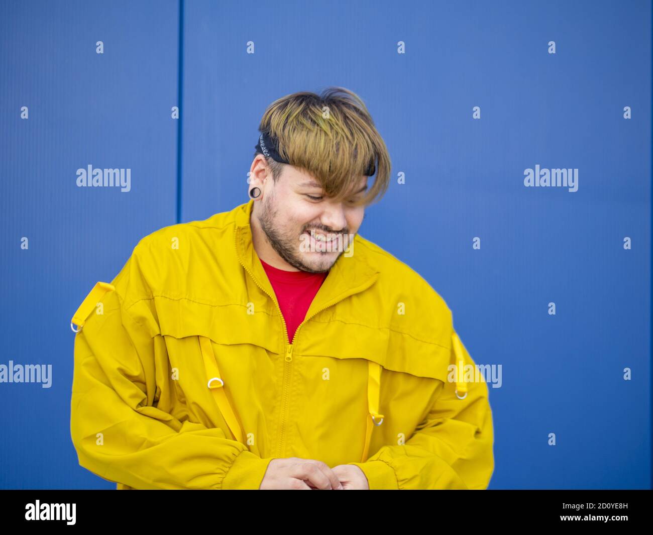 Male wearing a yellow jacket and posing by a blue wall Stock Photo - Alamy